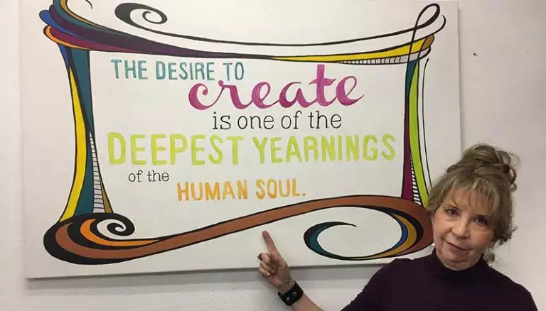Artistja e argjilës metalike Darlene Armstrong pozon pranë një shenje frymëzuese në studion e saj.